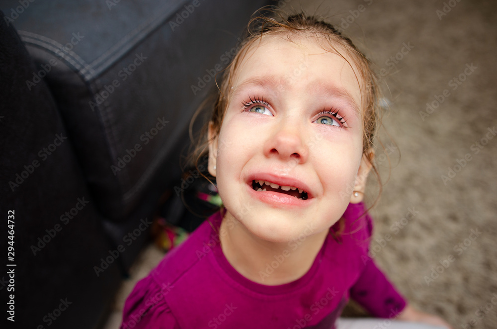 Little girl sitting on the floor, she is upset and crying. The child is ...