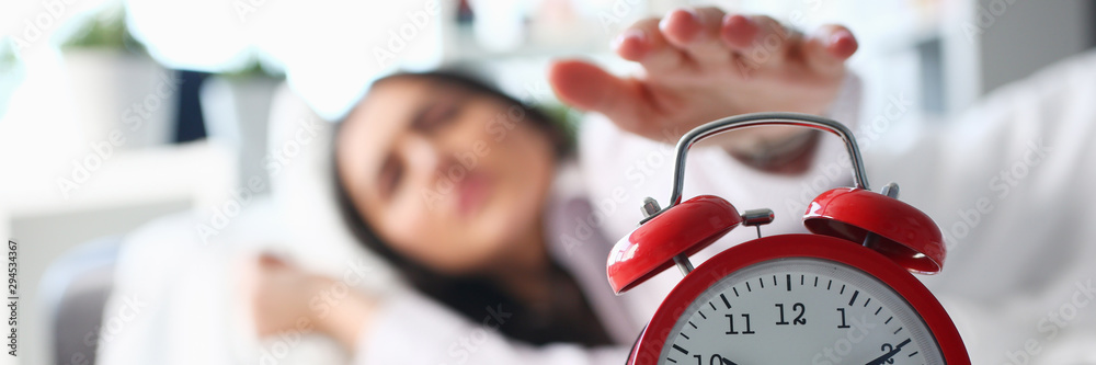 Sleepy young woman portrait with one opened eye trying kill alarm clock ...