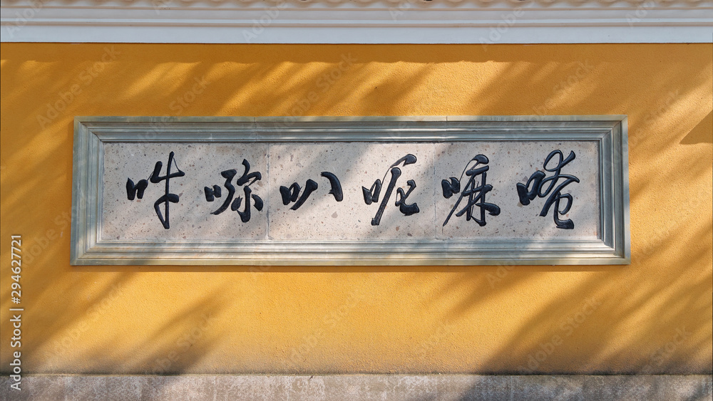 Yellow temple wall with mantra and sunny shadows, the six Chinese ...
