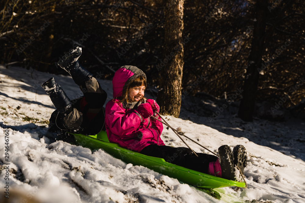little girl on a sled riding in the snow smiling, with another child ...