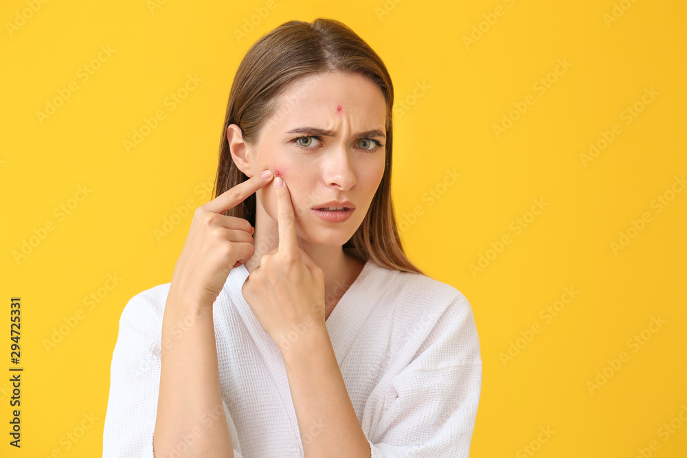 Portrait of young woman with acne problem squishing pimples on color ...