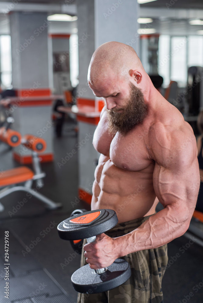 Brutal, muscular, bald with a beard athlete in the gym. Lifts heavy ...