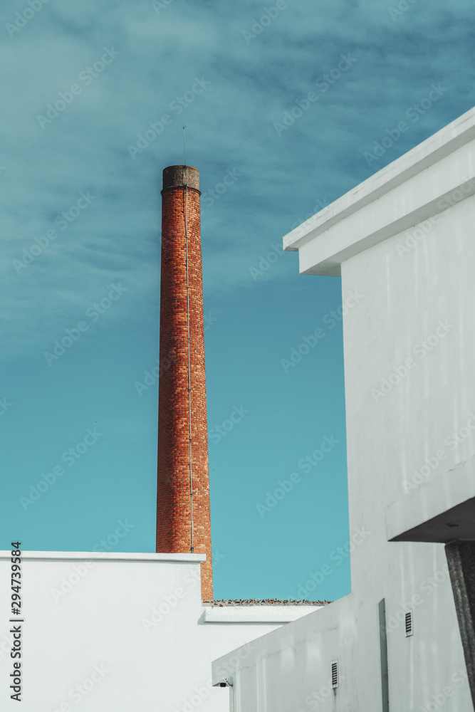 A vertical shot of a red brick funnel behind building roofs and white ...