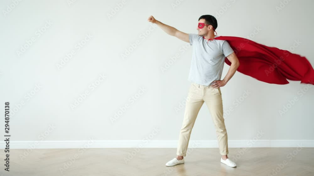 Portrait of super hero in fluttering red cape and mask standing with ...