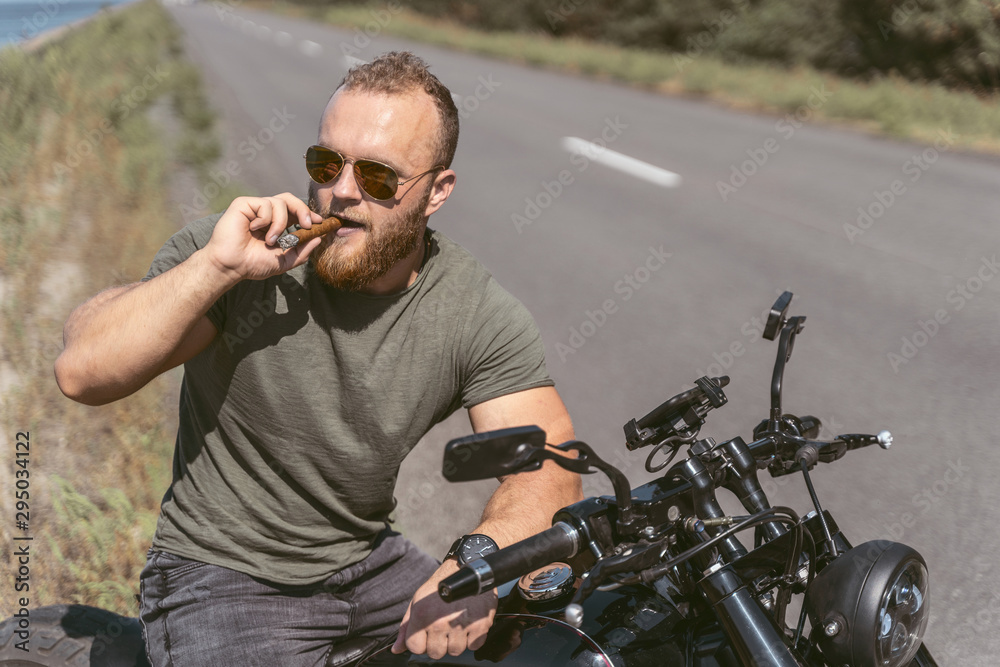 Attractive brutal biker sitting on bike smoking sigar at the side of ...