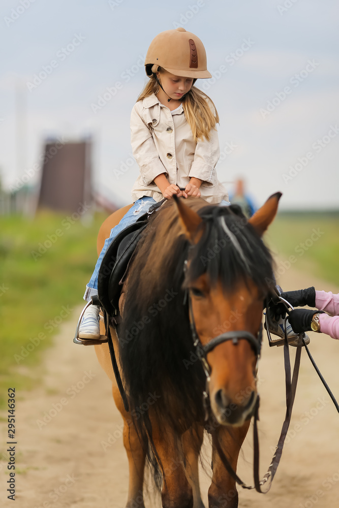 Little girl in an equestrian helmet riding a horse. Girl on a horse ...