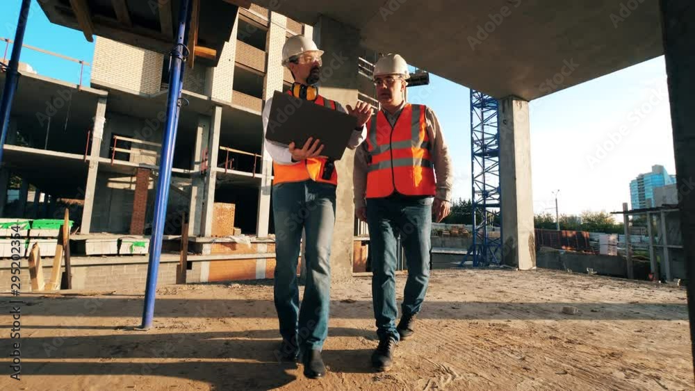 People walk on a construction site with a laptop. Construction workers ...