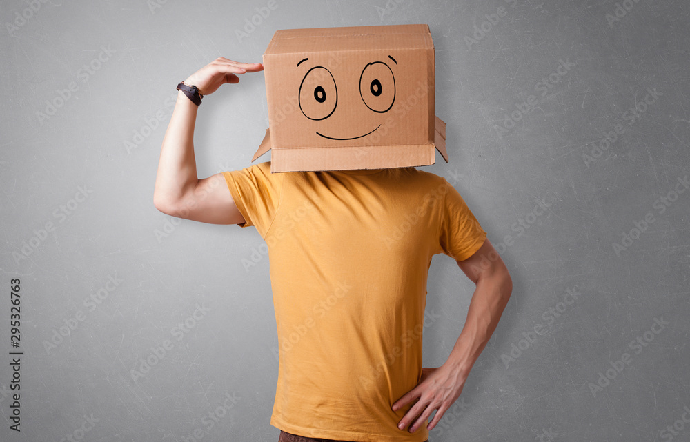 Young man standing and gesturing with a cardboard box on his head with ...