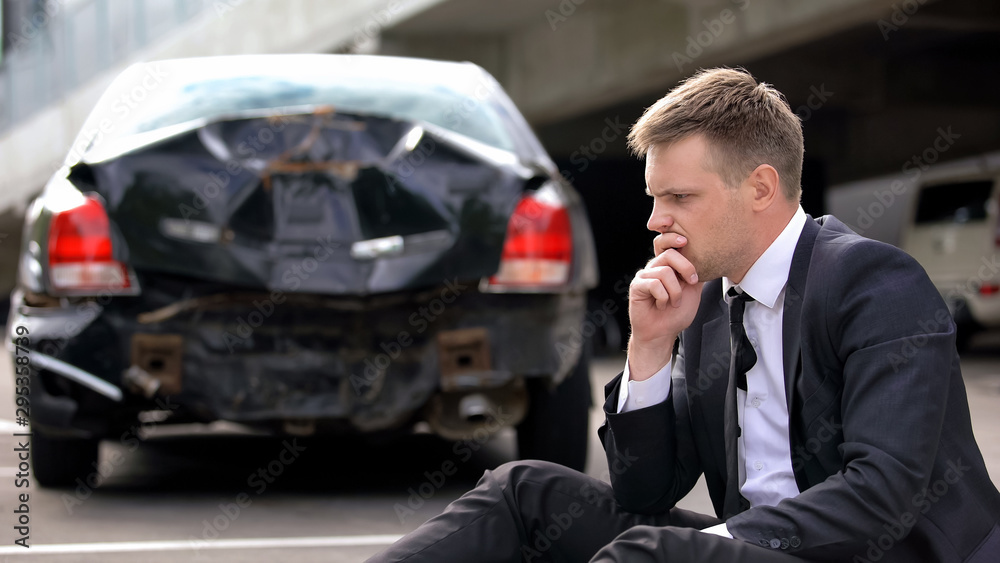Frustrated man sitting road on crashed car background, traffic accident ...