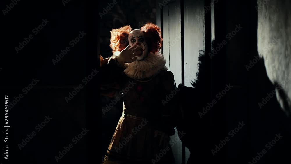 Vidéo Stock Scary clown with a crazy smile suddenly appears at the door ...