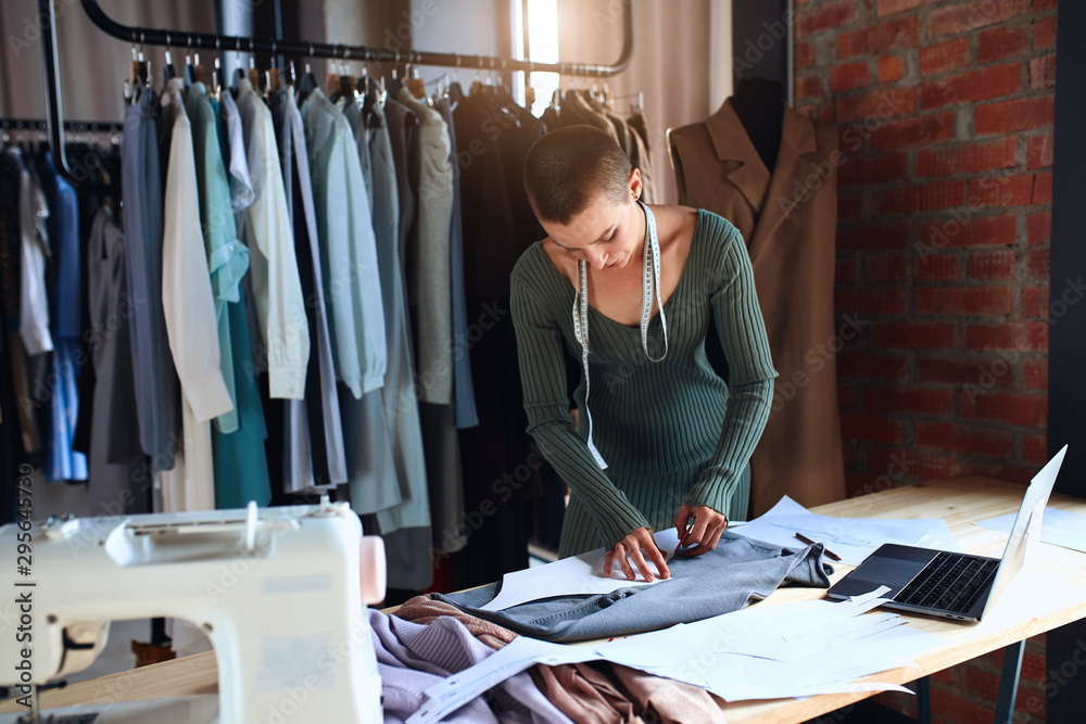 Female dressmaker sew new clothing in studio using laptop. Background ...