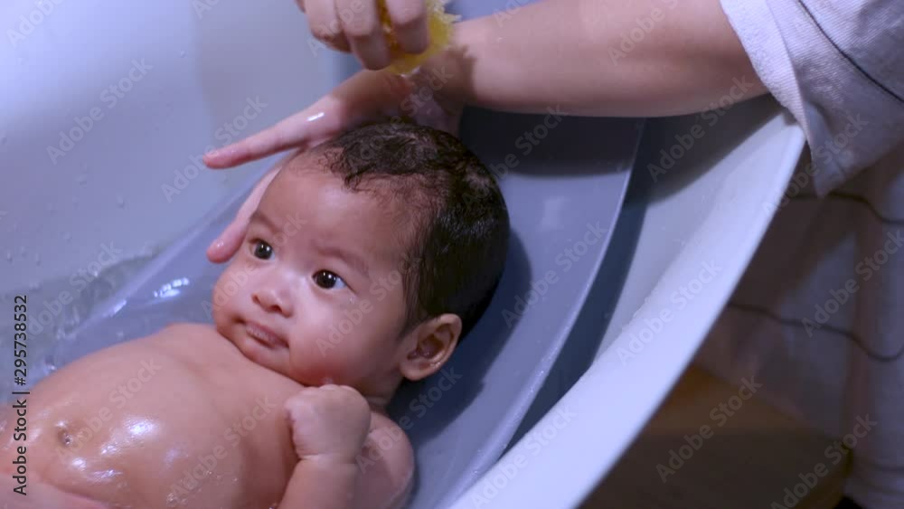 Asian baby infant lying on a bath tub, with a hand washing her hair at ...