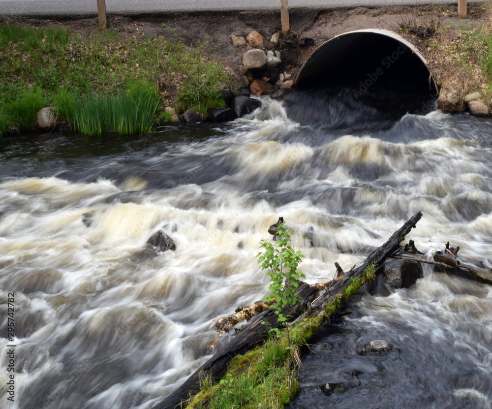 Flowing water out of a culvert under a road. Stock Photo | Adobe Stock