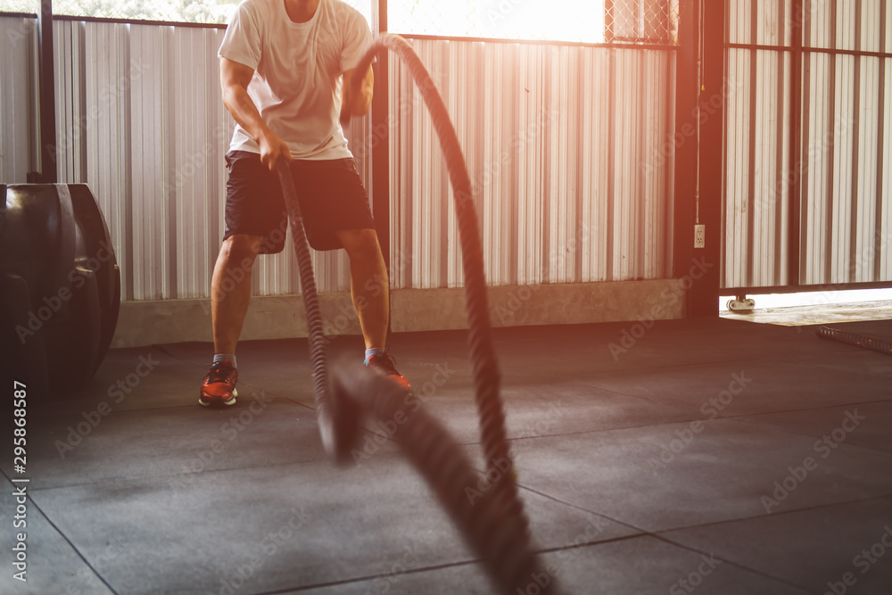 Athletic men doing a fitness workout with battle rope in functional ...