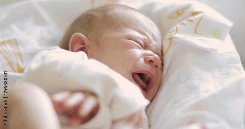 Portrait of sleepy sad newborn baby is crying in bed with closed eyes ...