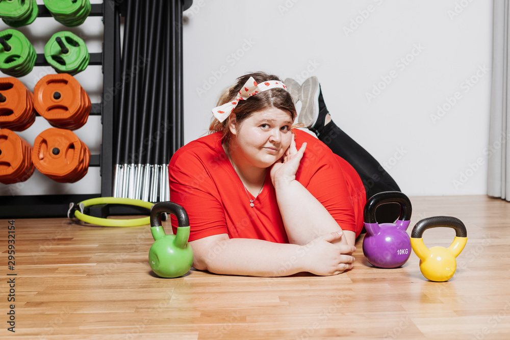 Fat and funny girl dressed in the sports wear is laying on the floor ...