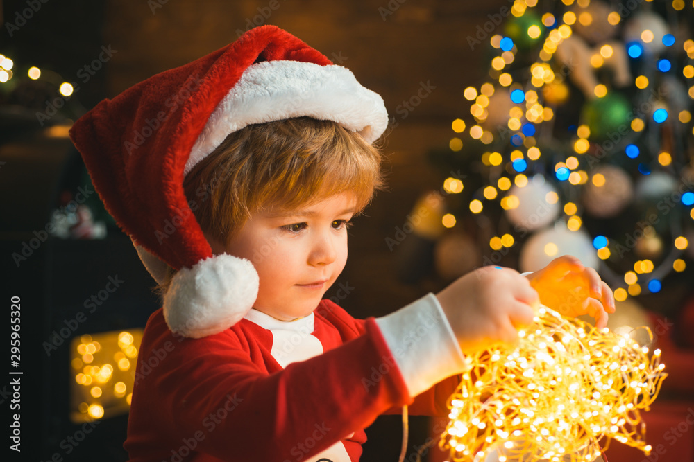 Child with garland lights at Christmas tree and fireplace on Xmas eve ...