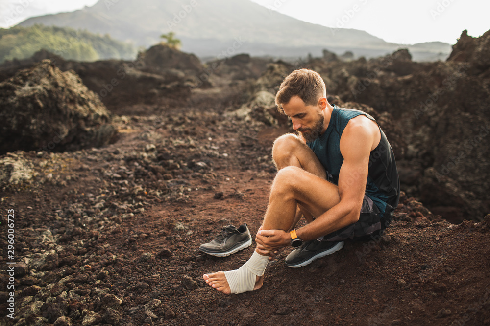 Male runner bandaging injured ankle. Injury leg while running outdoors ...