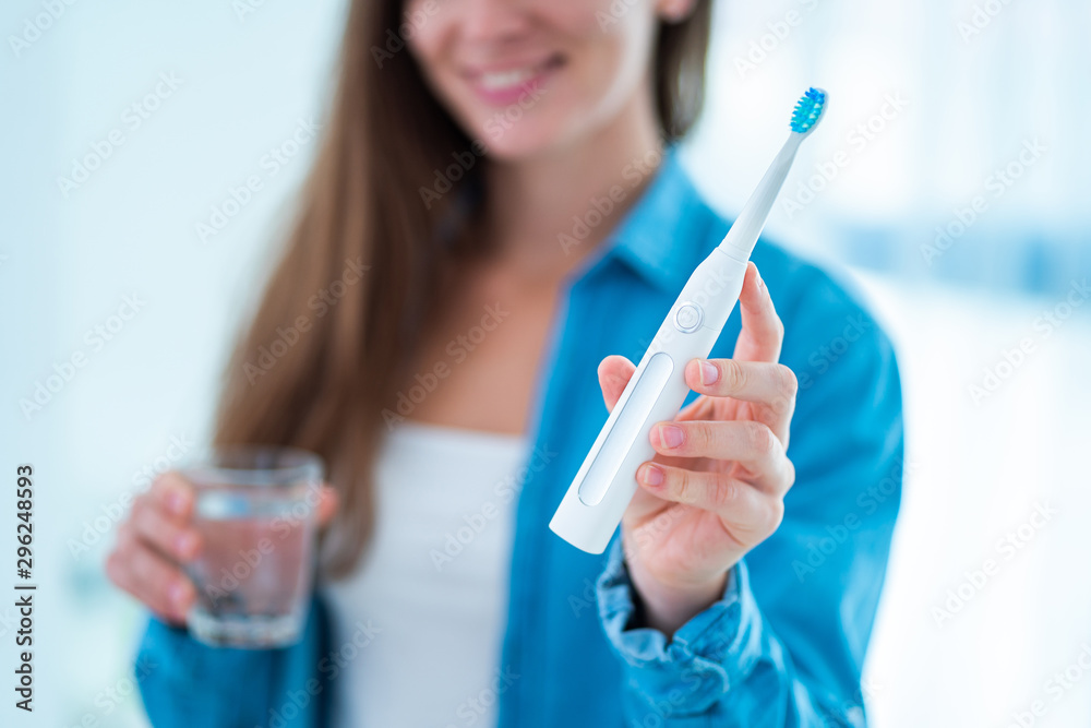 Happy smiling woman with ultrasonic electric toothbrush in bathroom at ...