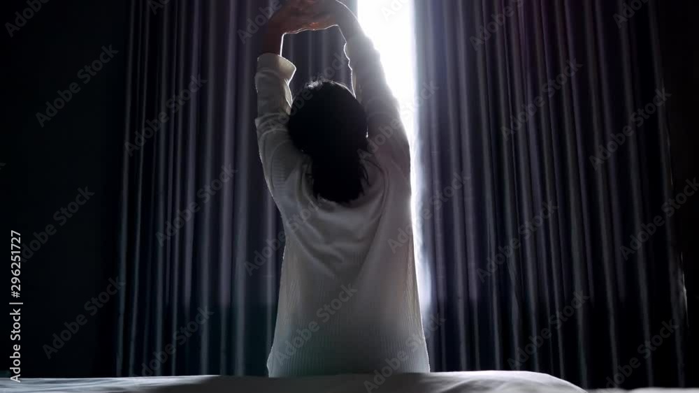 Rear of an Asian woman sitting and stretch lazily in the bright morning ...