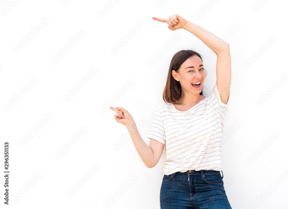 happy older woman with arms raised and pointing to empty space on white ...