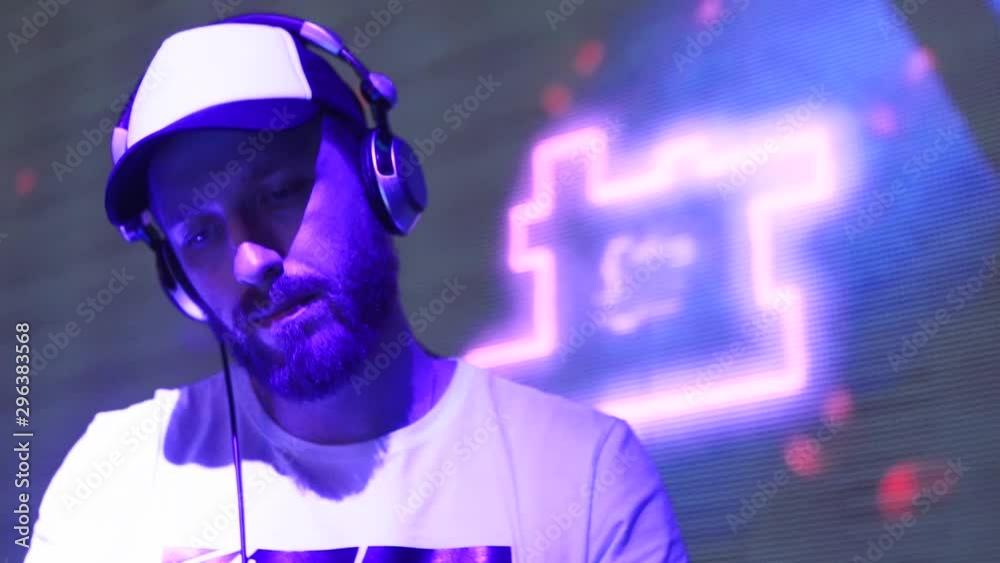 DJ performs on nightclub stage. Circular fly around bearded disc jockey ...