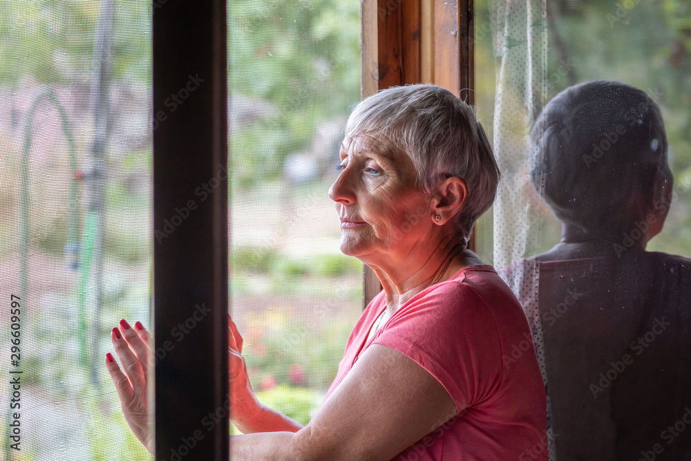 older woman with serious and sad expression looking out the window ...