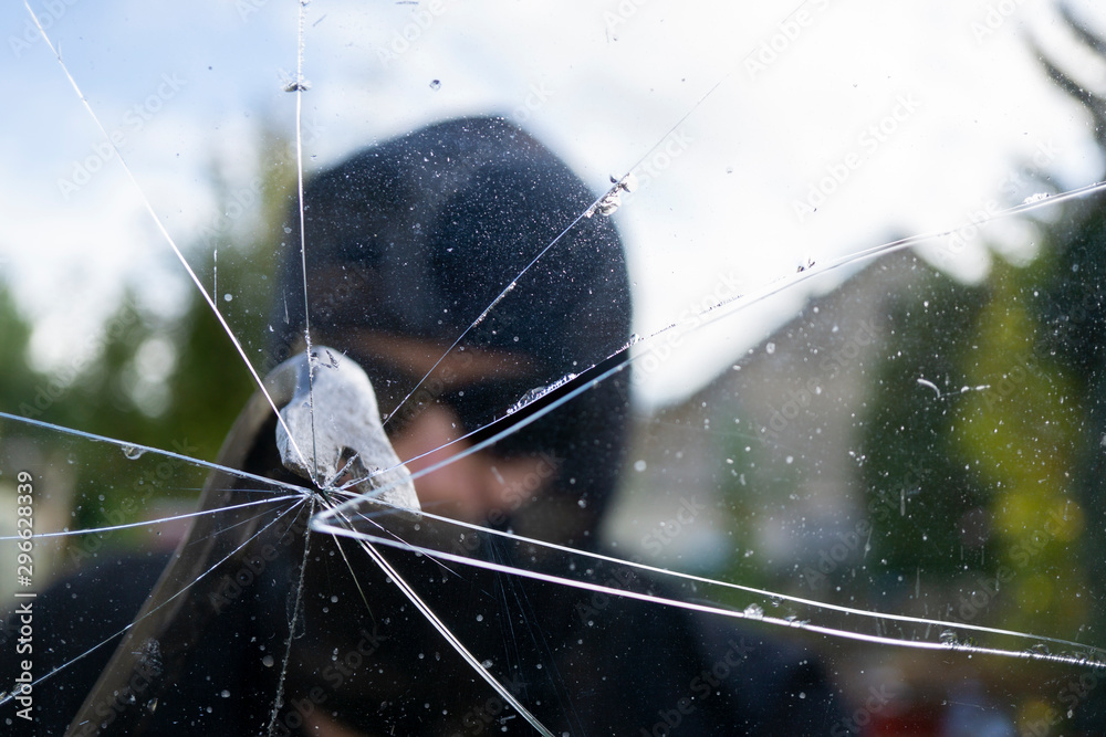 Burglar breaks the window. Burglar with obscured face trying to break ...