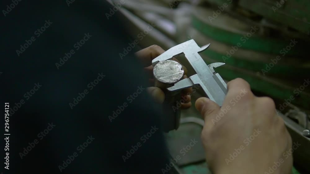 The hands of a factory worker are holding a metal detail and slide ...
