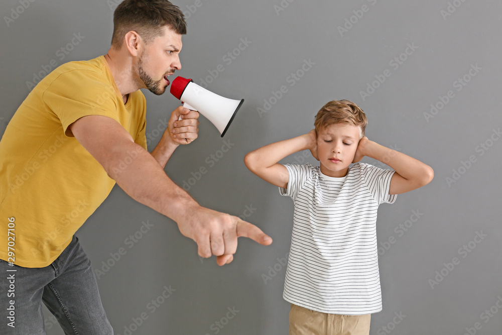 Little boy ignoring his angry father with megaphone against grey ...