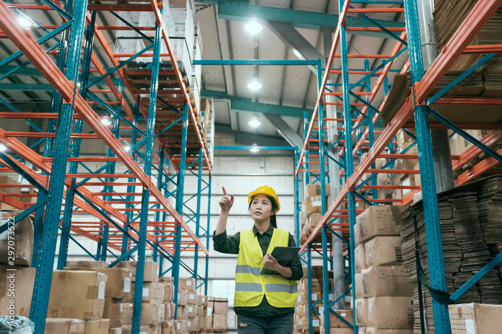 attractive young girl staff walking in large warehouse between shelves ...