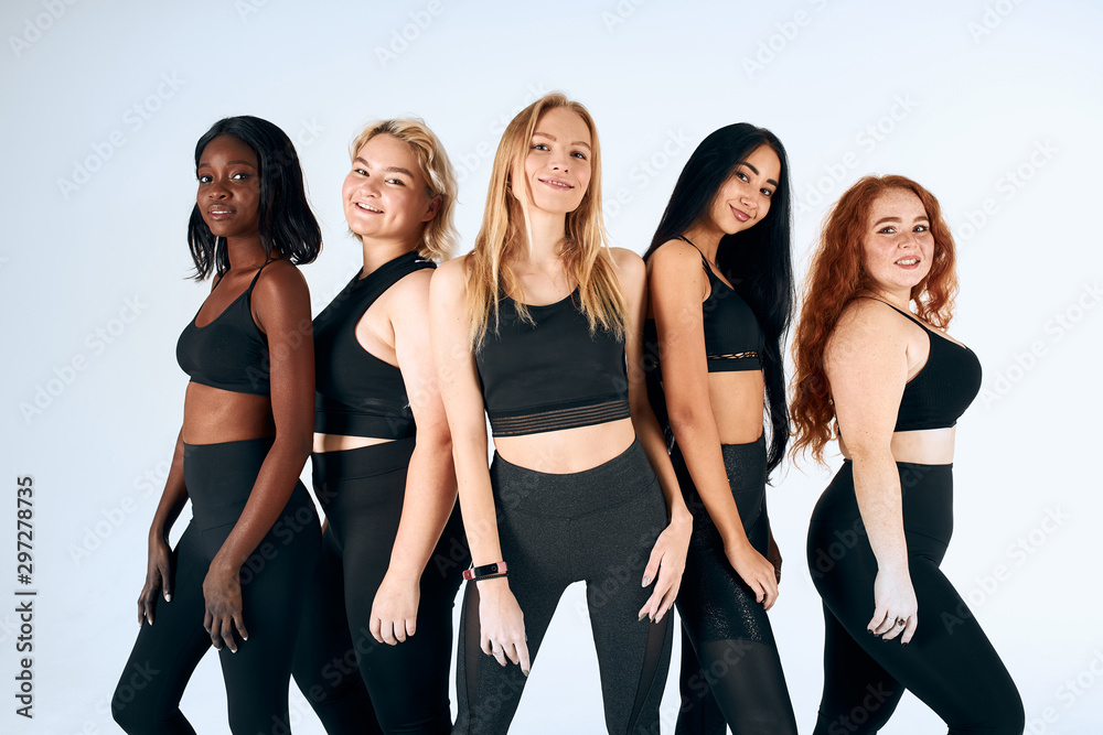 Young and positive girls of different nations stand smiling, look at ...