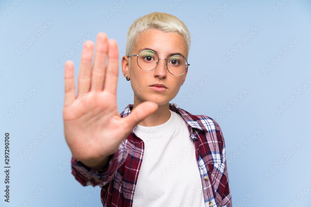 Teenager girl with white short hair over blue wall making stop gesture ...