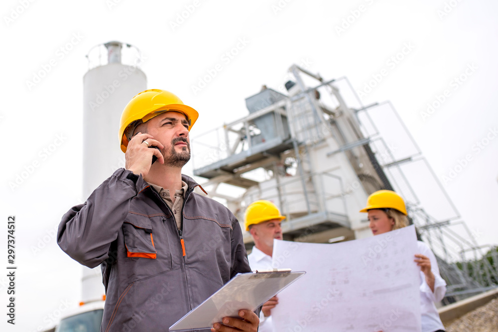 Civil engineer and colleagues on site, wearing safety helmet, checking ...