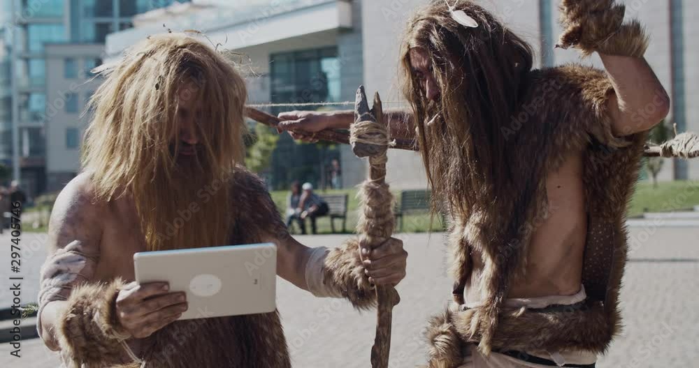 Angry caveman in animal fur using modern tablet browsing internet ...