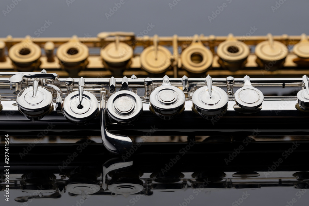 Two shiny gold and silver plated flutes on a reflective surface. An ...