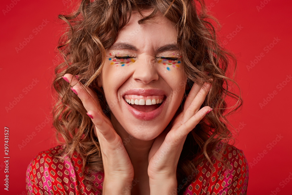 Pleasant looking curly lady with multicolored dots on her face laughing ...