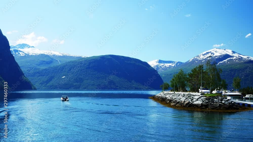A pleasure boat is slowly leaving Valldal, Norway on the calm waters of ...