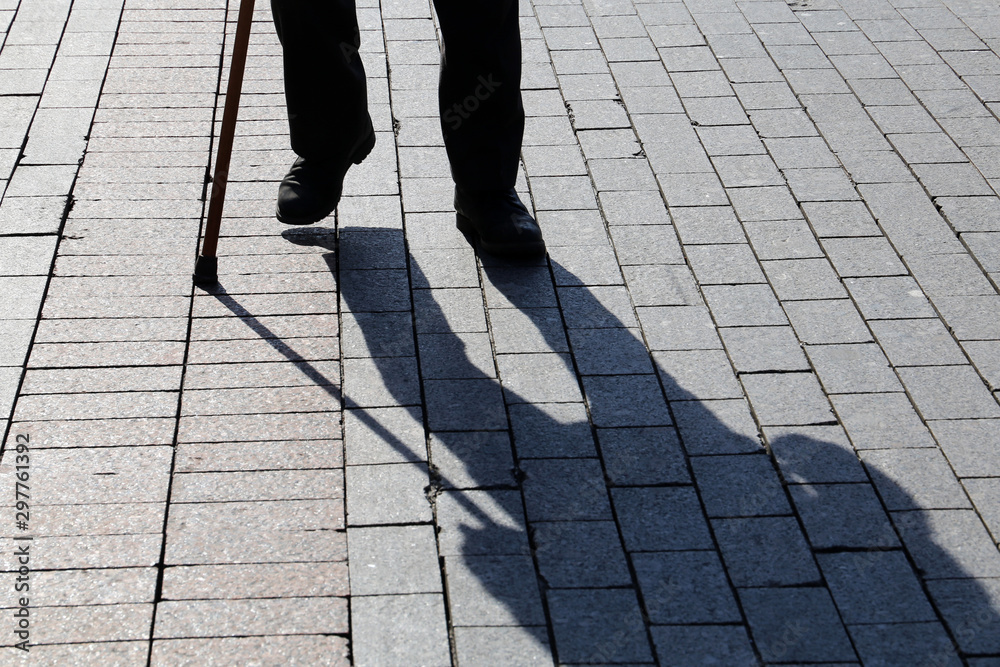 Shadow and silhouette of limping man walking with a cane on pavement ...