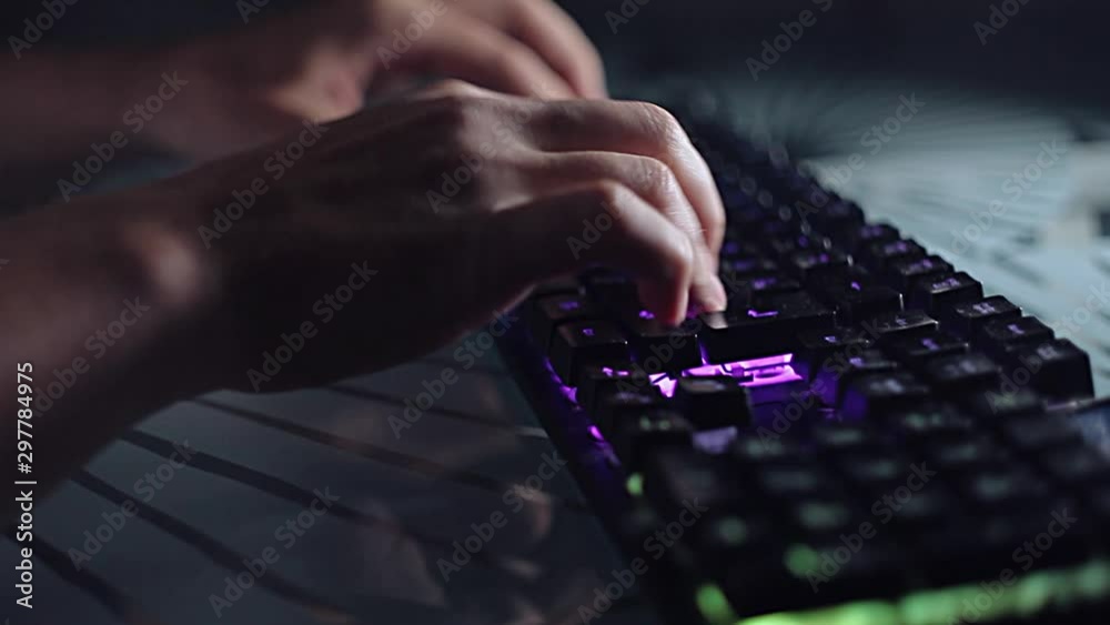 Programmer typing code on a backlit keyboard in a dark room, passionate work at the computer ...