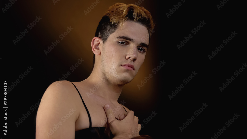 Transgender man in dress holding wig looking with sadness at camera ...