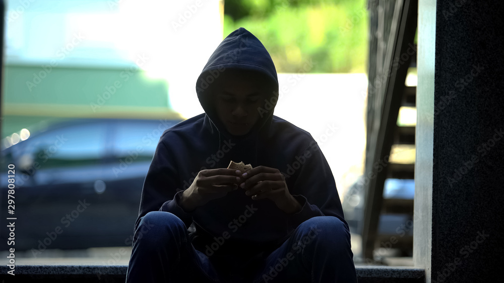 Homeless hungry guy eating sandwich sitting in darkness on stairs ...