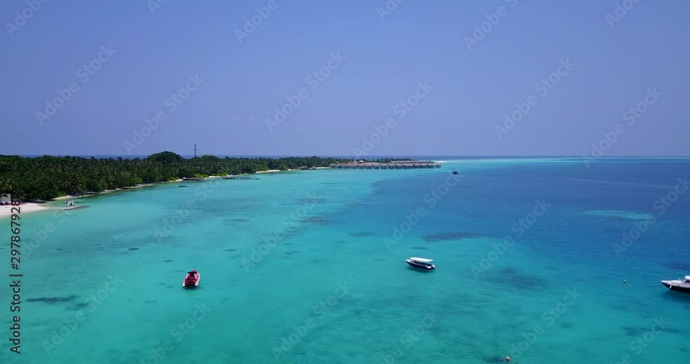 Flying slowly over clear bright teal water with some motor boats ...