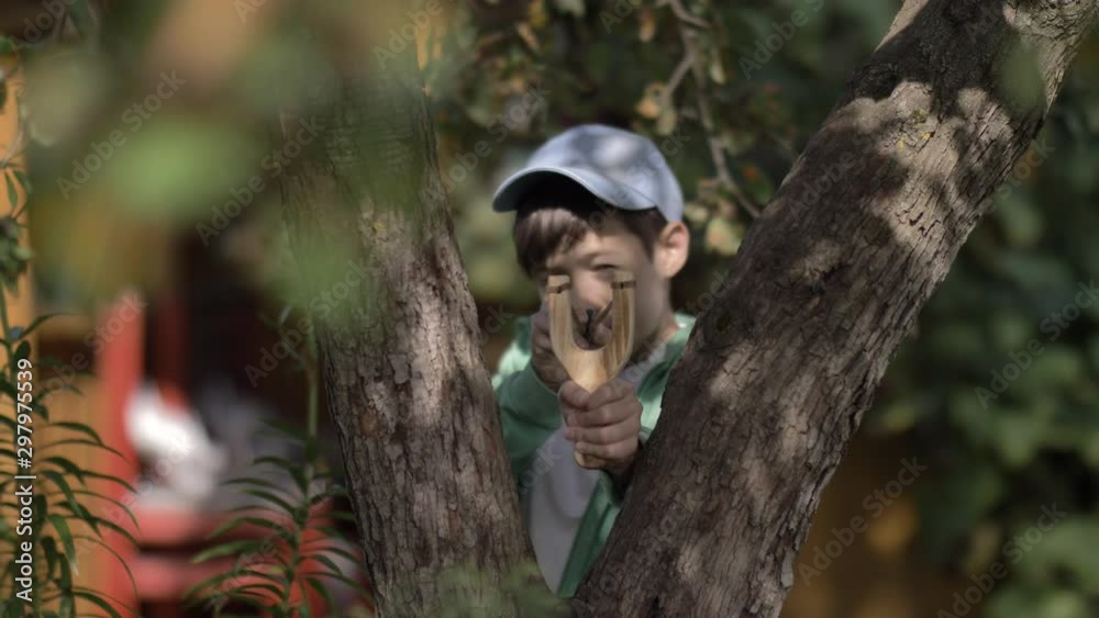 funny boy hides behind a tree and aims with a slingshot outdoors Stock ...