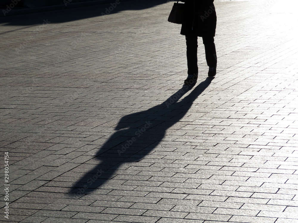 Silhouette and shadow of lonely woman with handbag walking on a street ...