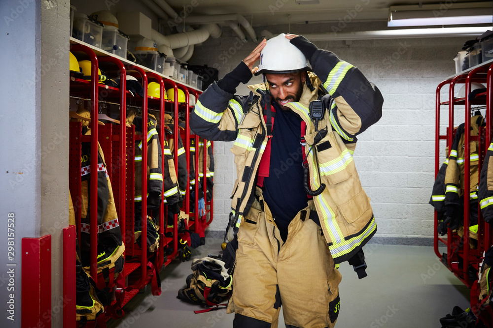 Mid adult firefighter wearing work helmet in locker room at fire ...