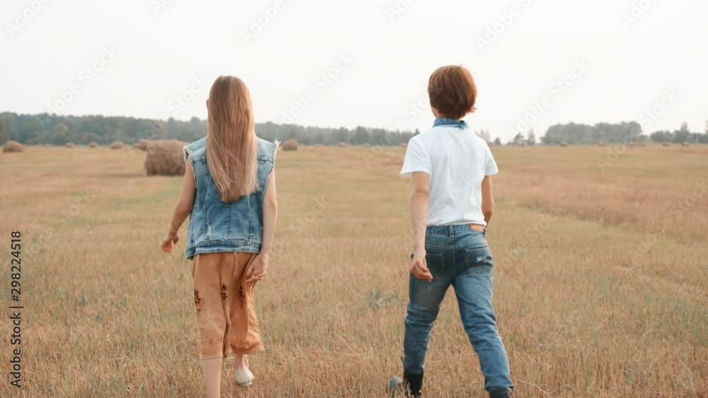 Back view of two stylish teens walking together in rural field. Rear ...