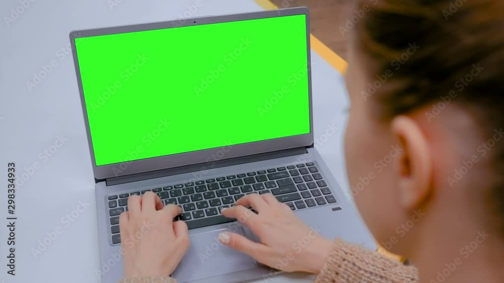 Over shoulder view - woman sitting at table and typing on laptop ...