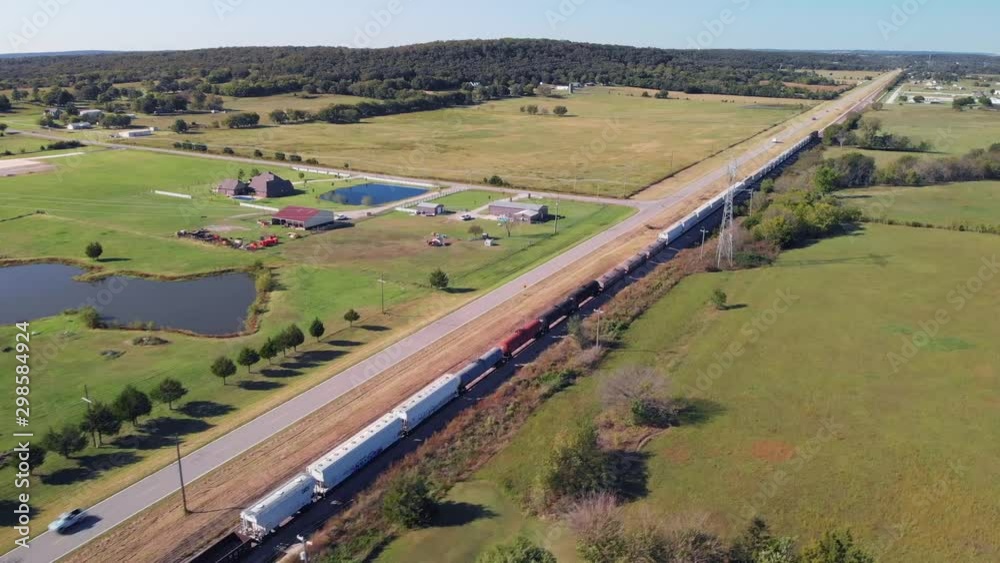 A long train driving through the country on a clear day near a 1 lane ...