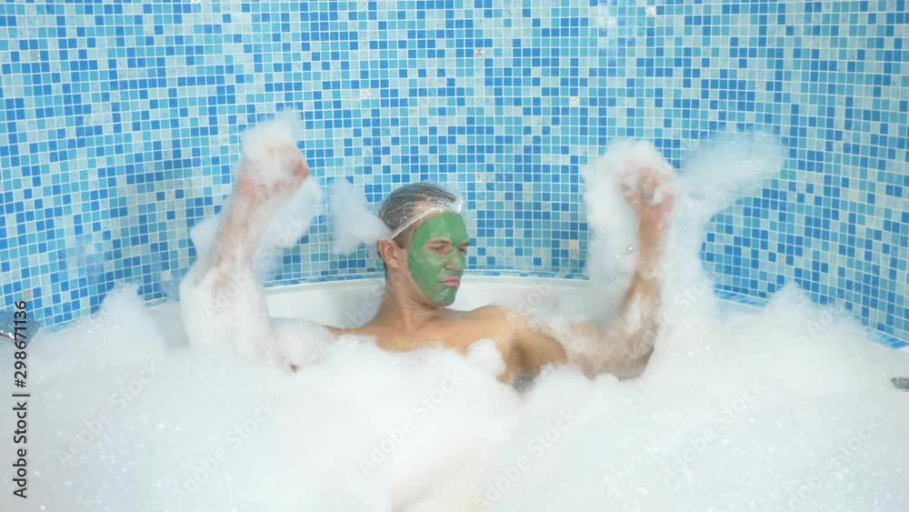 A young man with a green mask on his face and in a shower cap takes a ...
